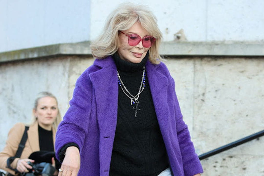 Amanda Lear en manteau long violet et jean blanc ample au défilé Paco ...