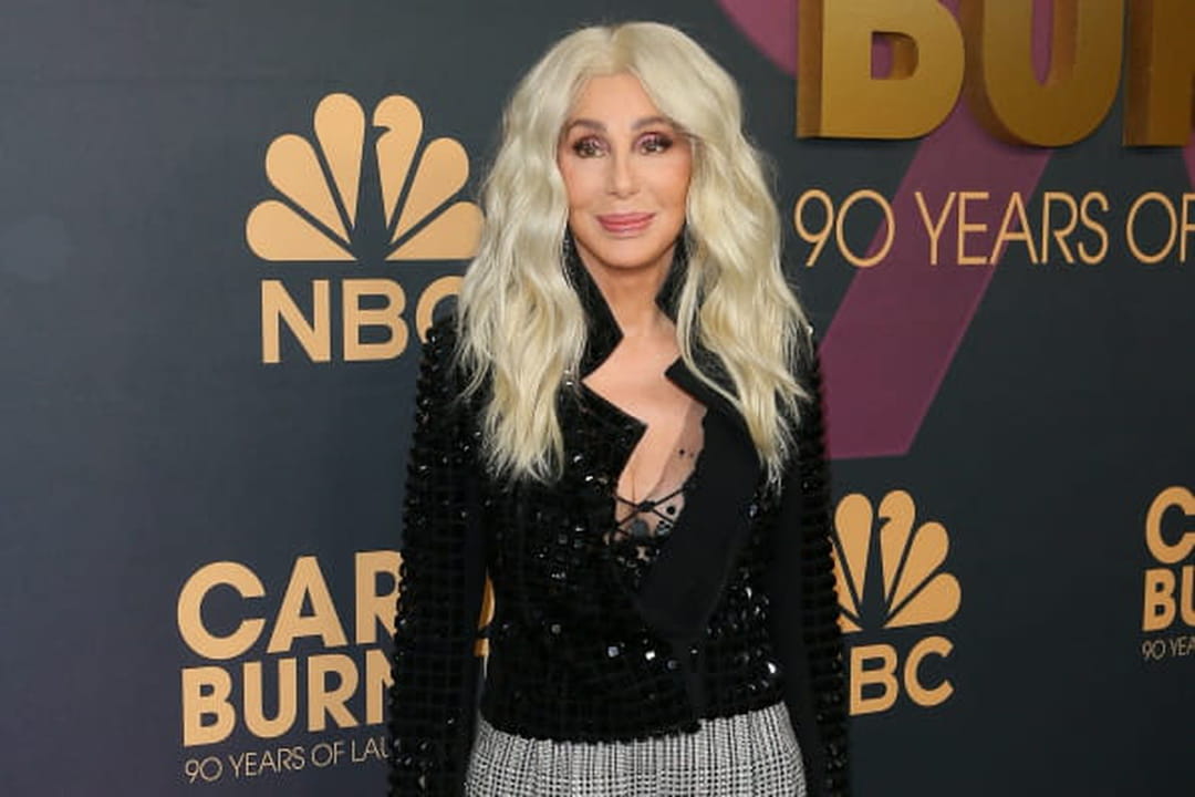 Cher en pantalon gris à rayures et veste noire